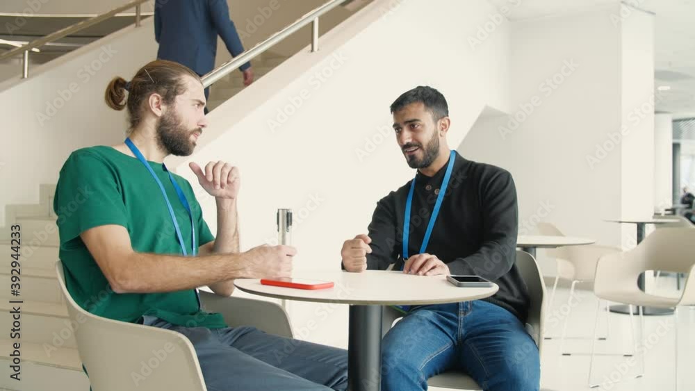 Young workers talk during their lunch break in office. Media. Two colleagues with badges are ...