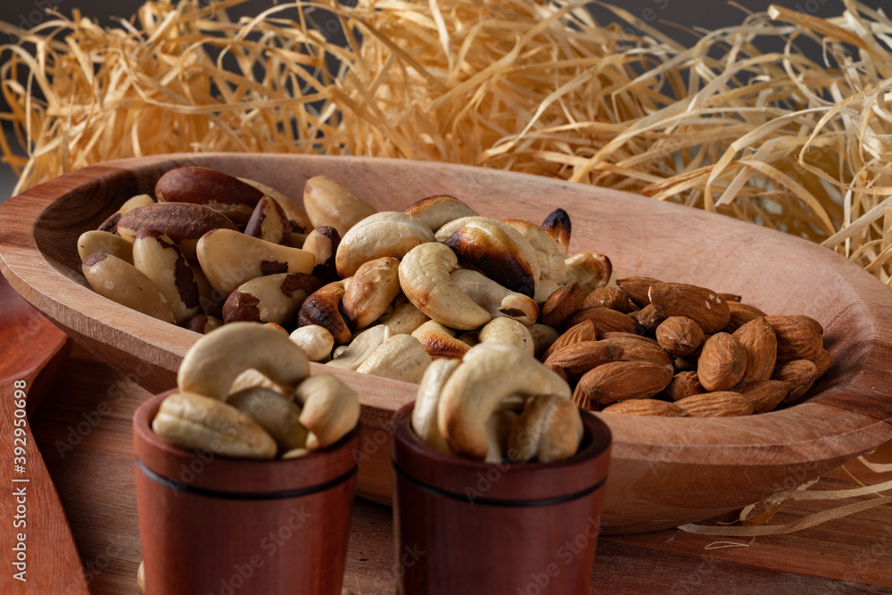 variety of nuts in a wooden bowl and in two wooden cups with straw ...