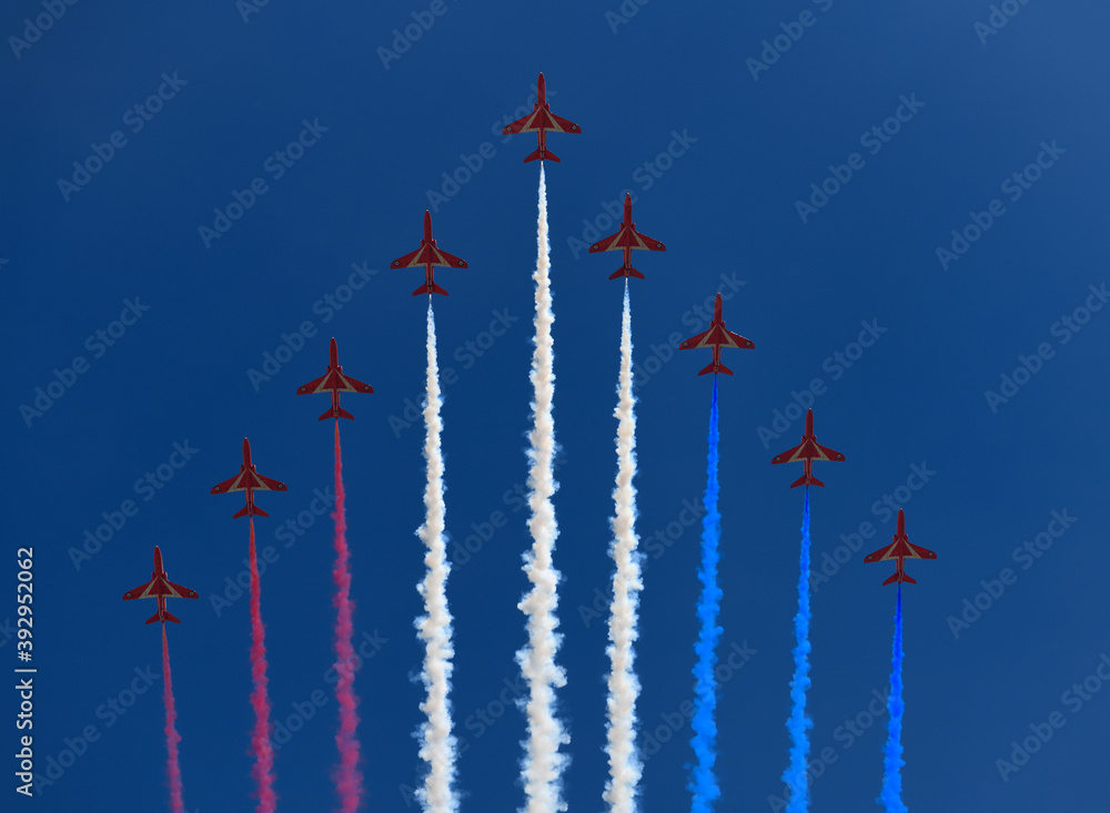 Formation of RAF Red Arrows with coloured trails on blue sky for ...