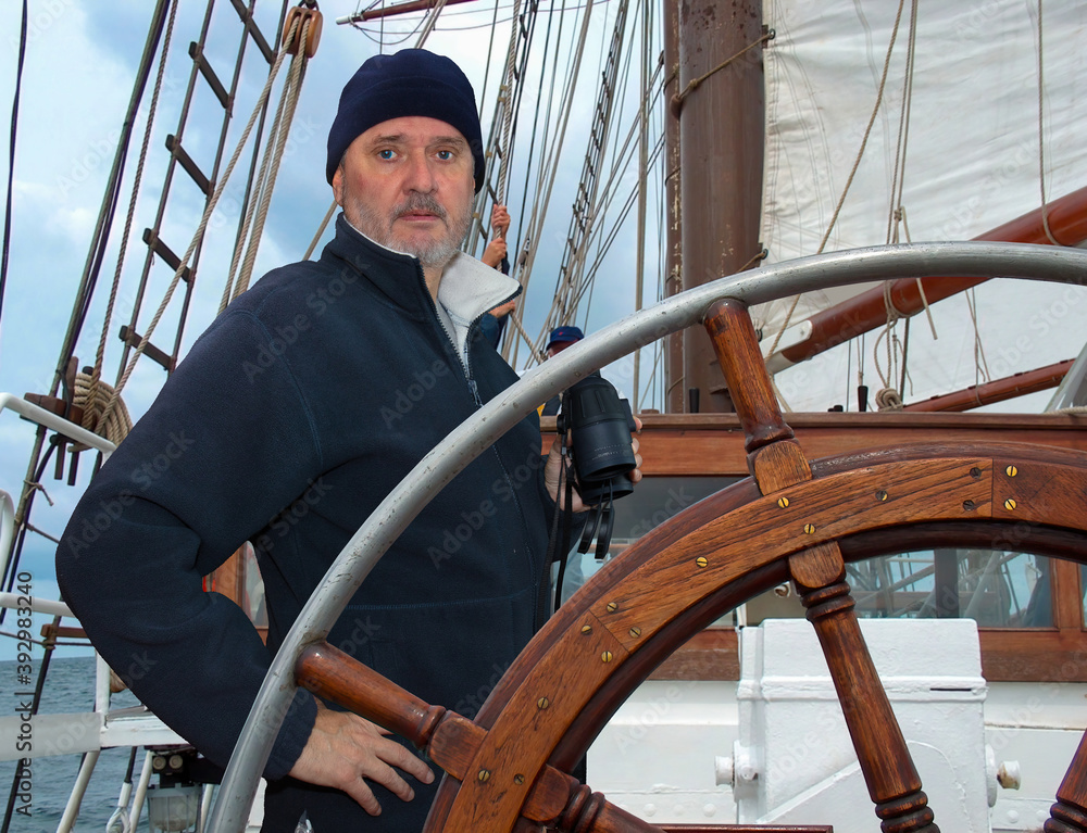 A captain of a large historic sailing ship behind the wheel. He has ...