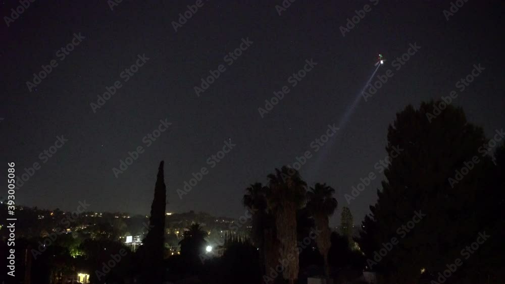 Police helicopter searches from the city night sky with a spotlight ...