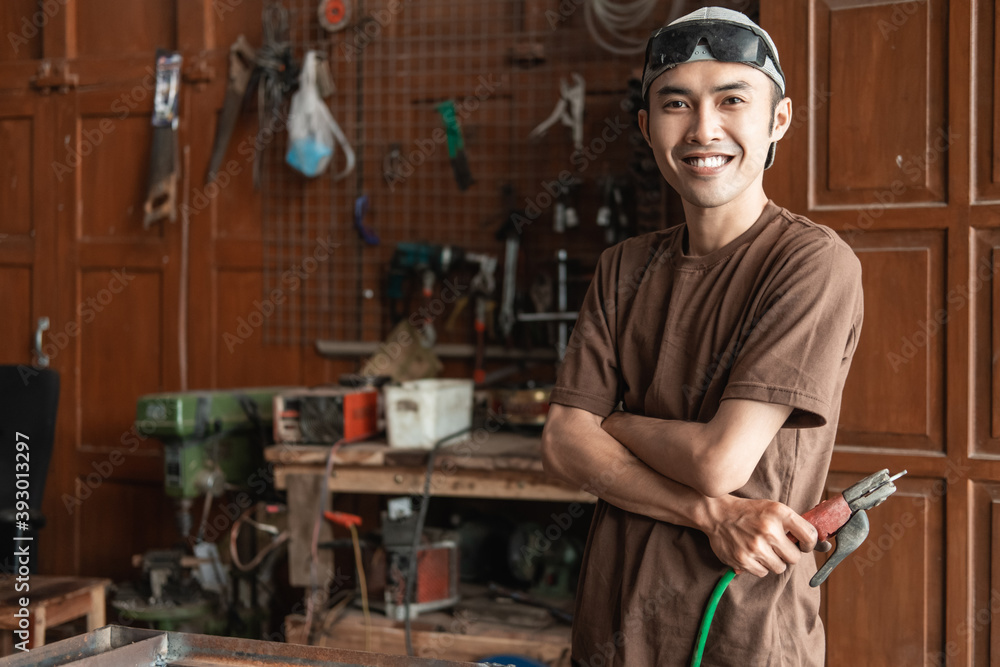 Male welder smiles with crossed hands while holding electric welder in ...