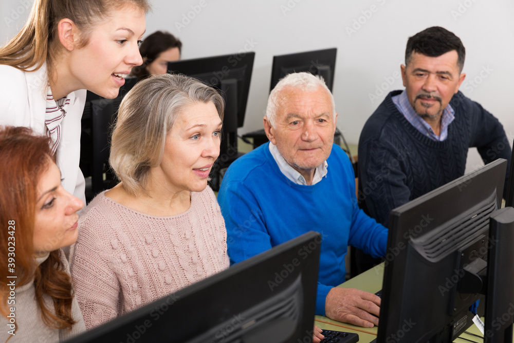Group of smiling students of different ages looking together at monitor ...