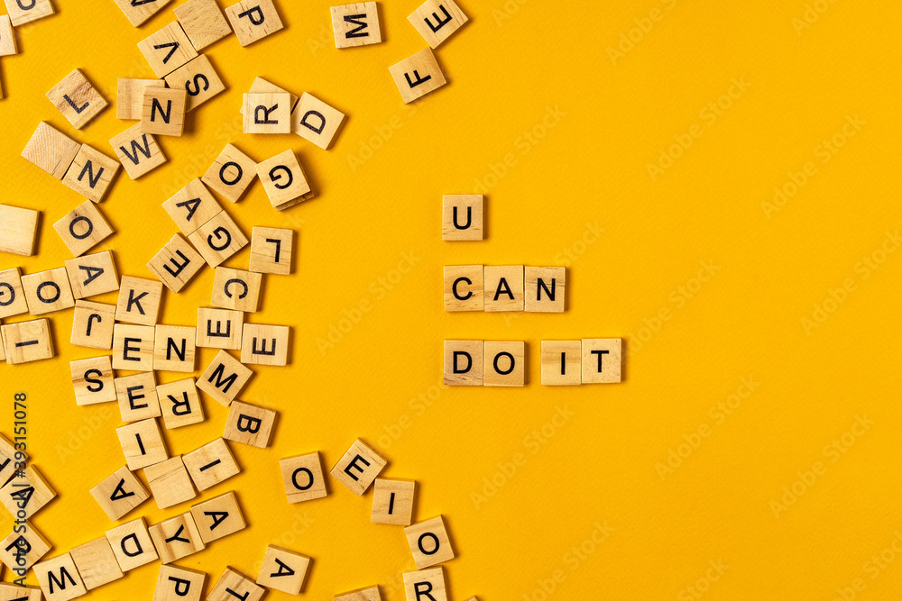 The word "YOU CAN DO IT" is made of wooden letters on a bright yellow ...