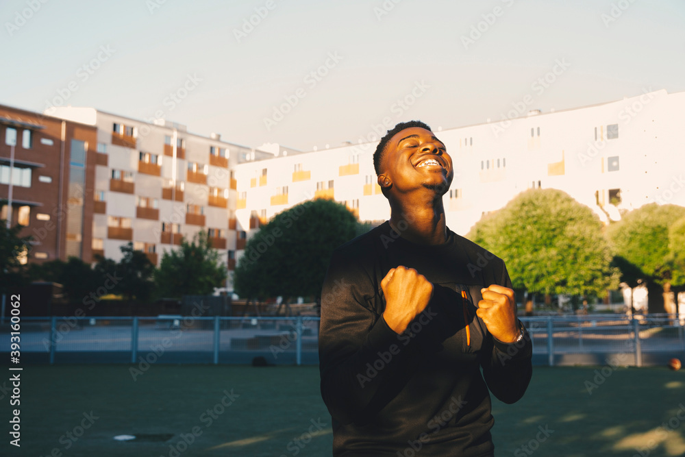 Smiling young man cheering with eyes closed in sports field Stock Photo ...