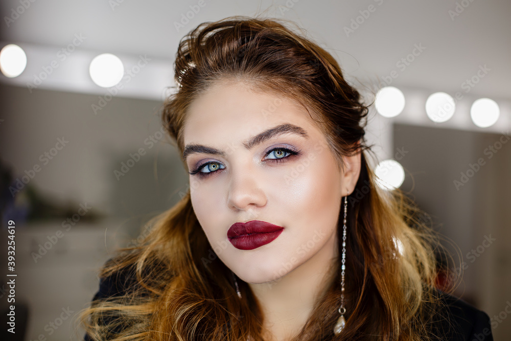 Young woman with bright makeup in dressing or makeup room near mirror ...