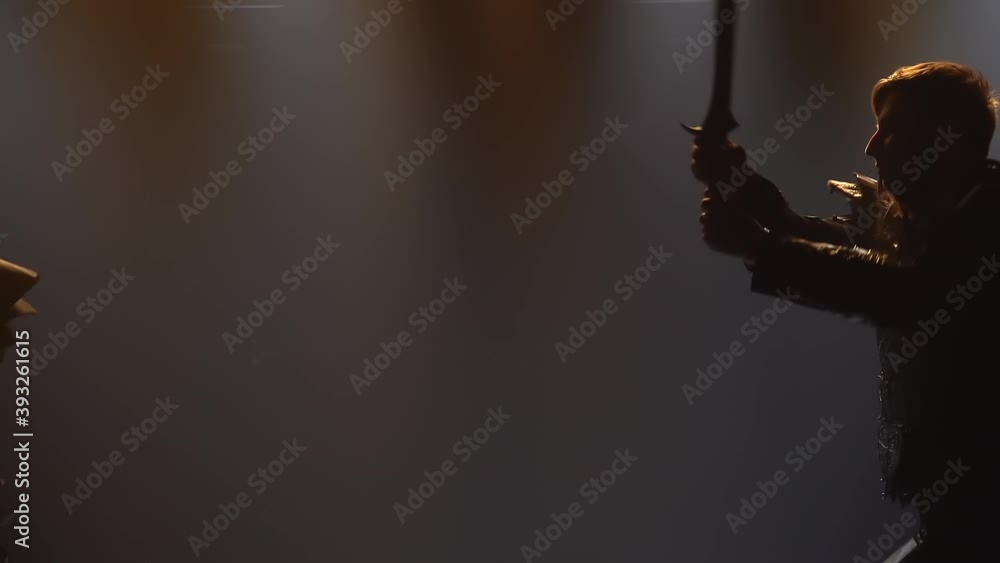 Men fight with swords in a dark studio with stage lighting. Silhouettes ...
