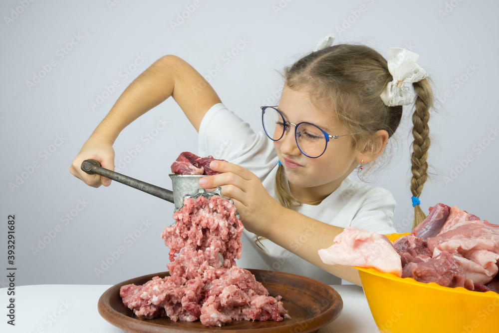 little girl with glasses scrolls through fresh raw meat making minced ...
