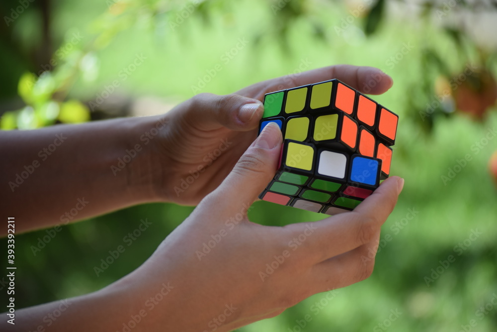 Rubik's cube in hand trying to solve, close up side on a green ...
