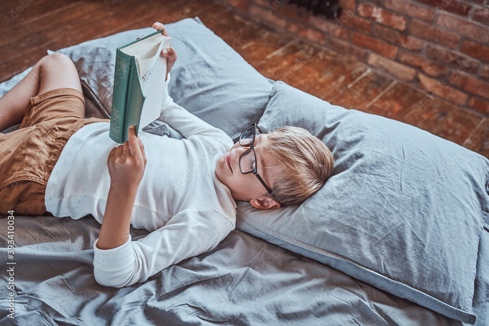 Portrait of joyful preschool child with glasses reading a book and ...