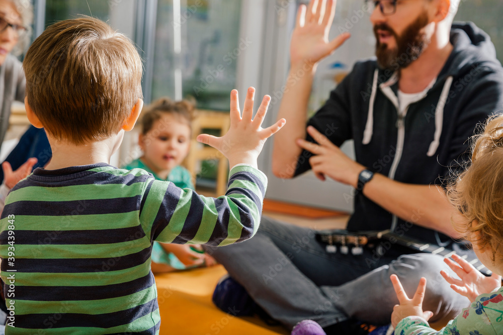 Child raising hand while singing with others and teacher in ...