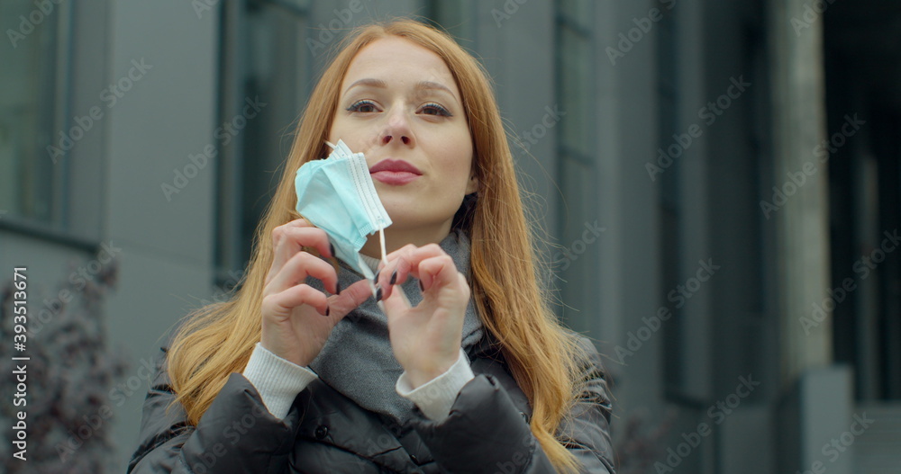 Young redhead woman taking off protective mask against COVID virus ...