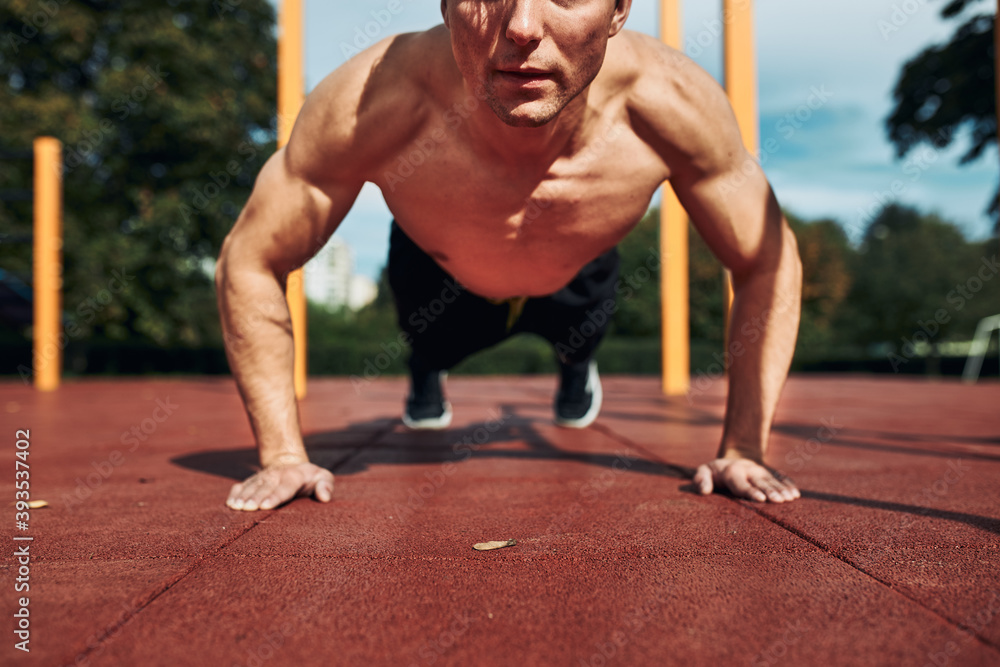 Young shirtless man bodybuilder doing push-ups on a red rubber ground ...