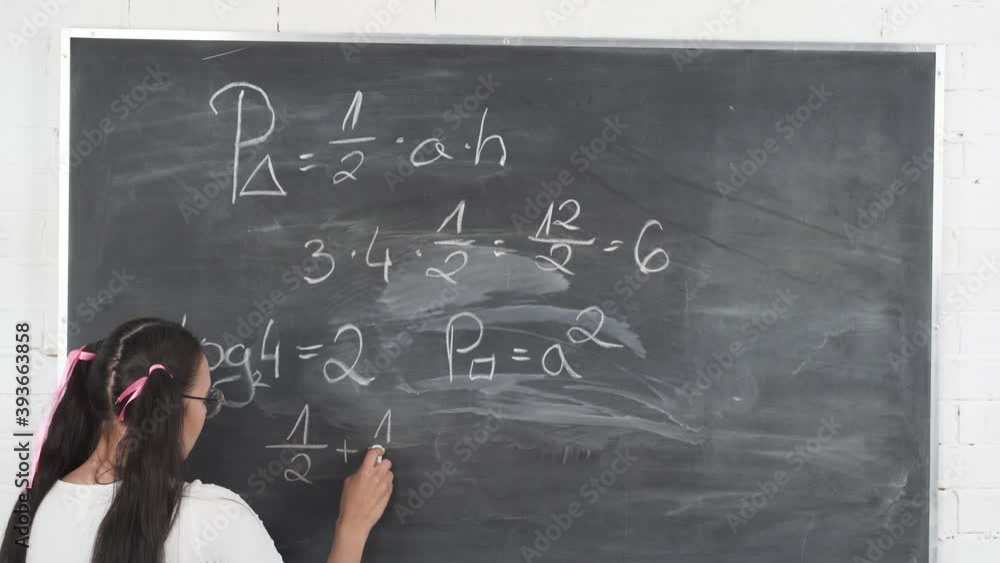 Teenager chalks a math equation on a dark gray school blackboard. Her ...
