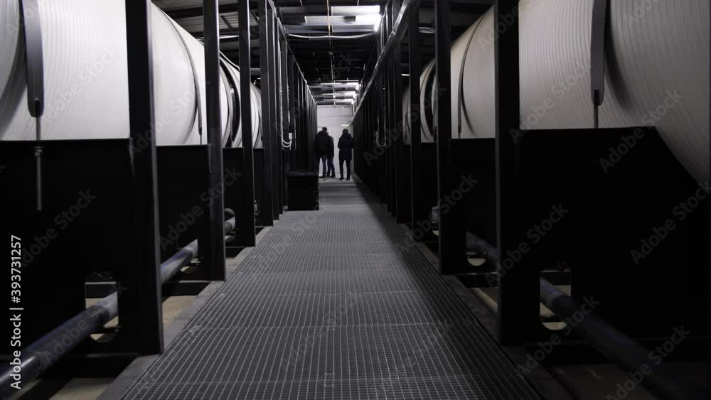 Rear view of three men walking along water treatment tanks at the power ...