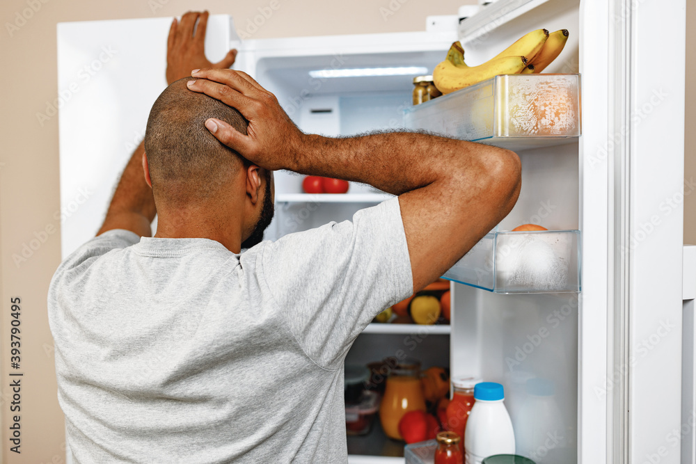 African american man standing in front of open fridge and choosing food ...