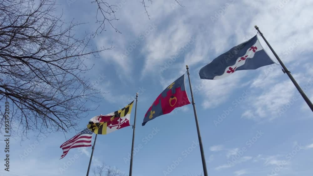 Four flags are vawing on seperate flags poles against blue sky on a ...