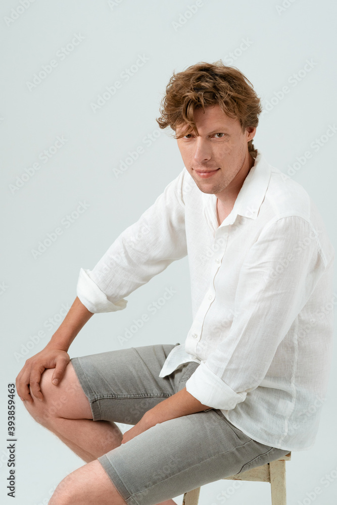 Sitting on chair young man looking at camera isolated on white ...