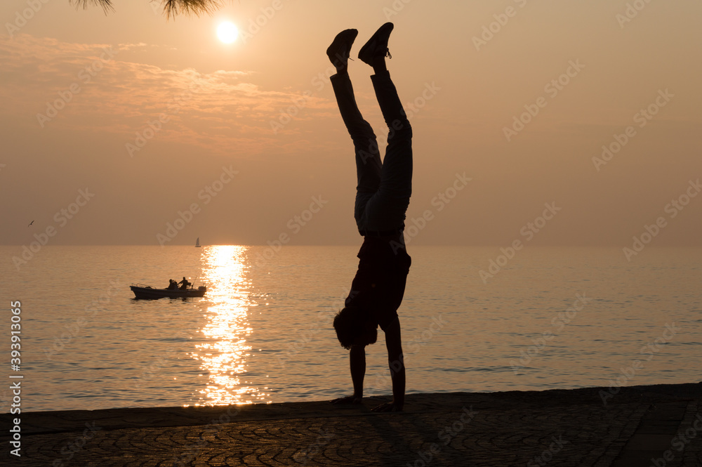 Silhouette of a young man handstanding in front of the sea at suset ...