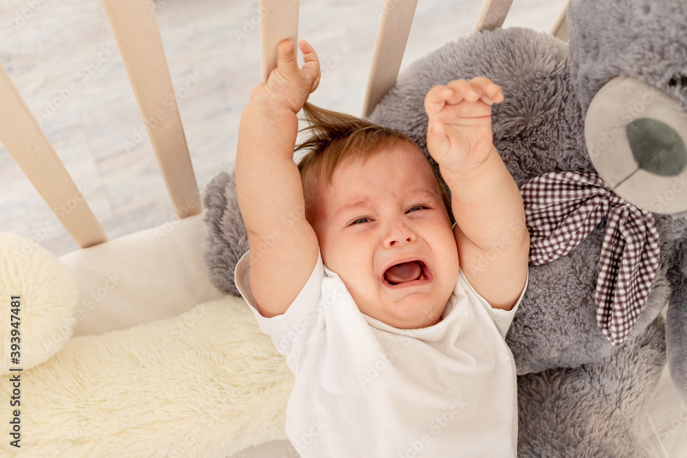 baby boy six months old crying in his crib with a big Teddy bear Stock ...