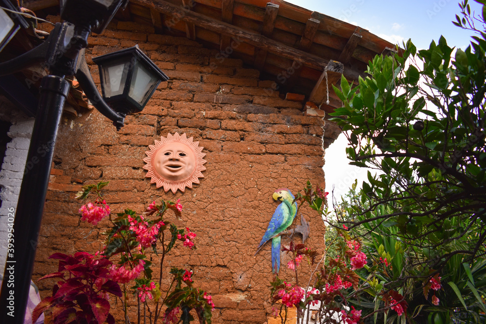 Pared de adobe con un sol y un perico como adorno en un jardín. foto de ...