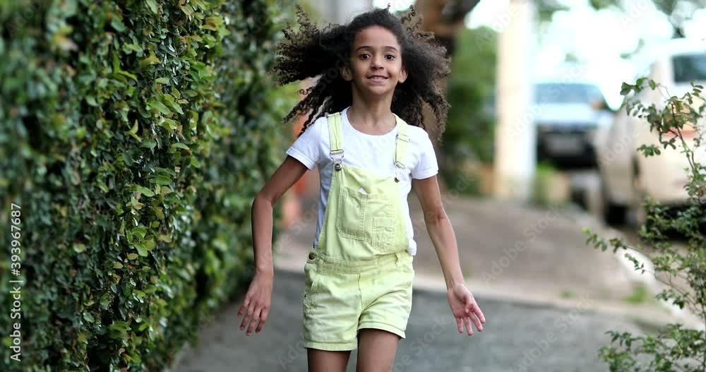 Happy little girl hopping outside in city sidewalk. Mixed race kid ...