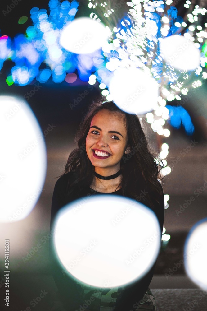 Portrait Of Smiling Teenage Girl Sitting Against Illuminated Lens Flare ...