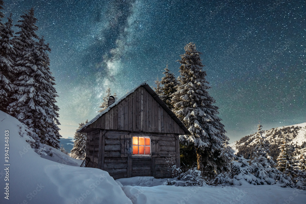 Fantastic winter landscape with wooden house in snowy mountains. Starry ...