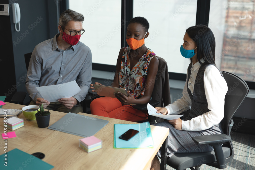 Diverse colleagues wearing face masks laughing together at modern ...