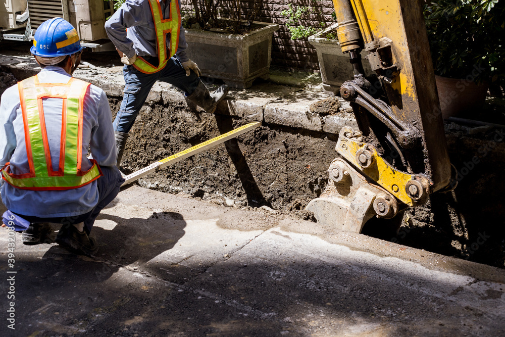 A backhoe and crew dig a utility trench for gas and other electrical ...