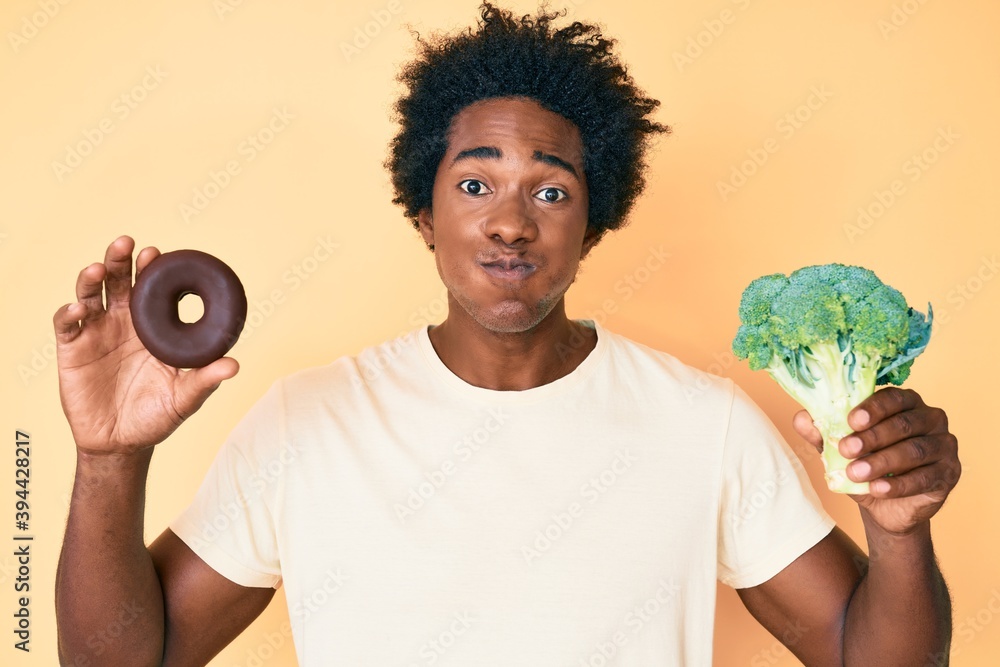 Handsome african american man with afro hair holding broccoli and ...
