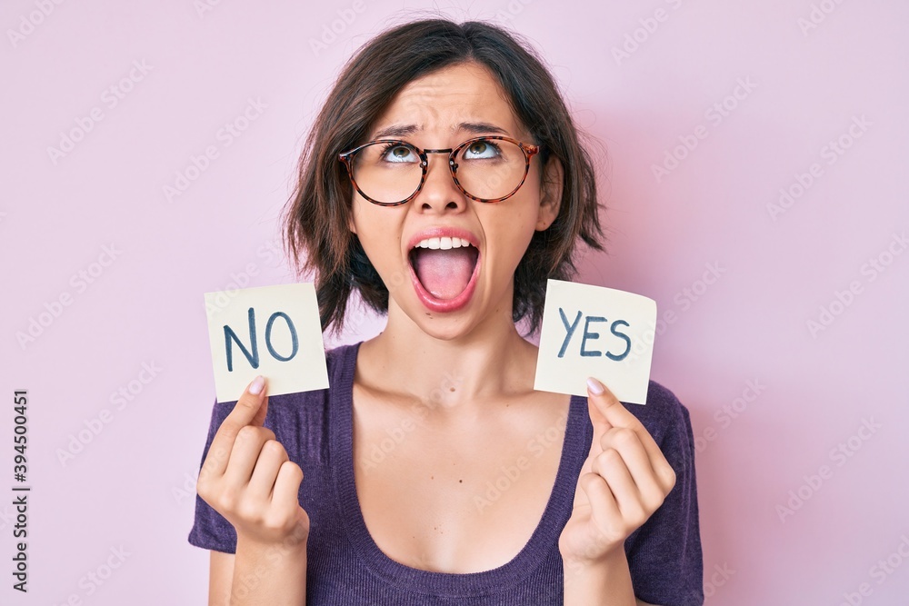 Foto de Young beautiful girl holding yes and no reminder angry and mad ...