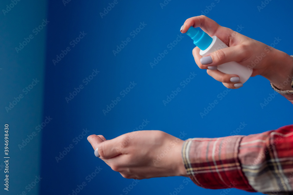 Woman spraying antiseptic on hands against blue wall - close up side ...