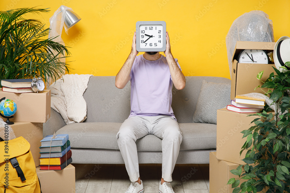 Young owner man hiding cover face with clock sits in living room on ...
