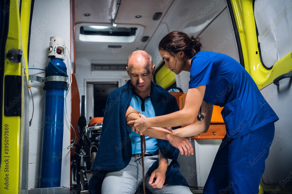 Paramedic wraps a tourniquet around the hand of an injured man in an ...