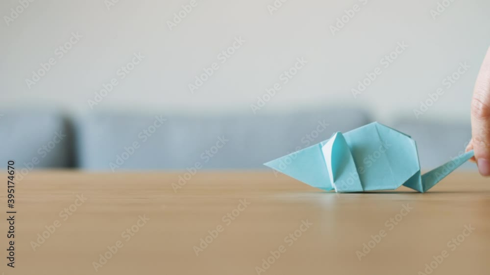 A hand moving a cute stylized blue handmade Origami Mouse on a wooden ...