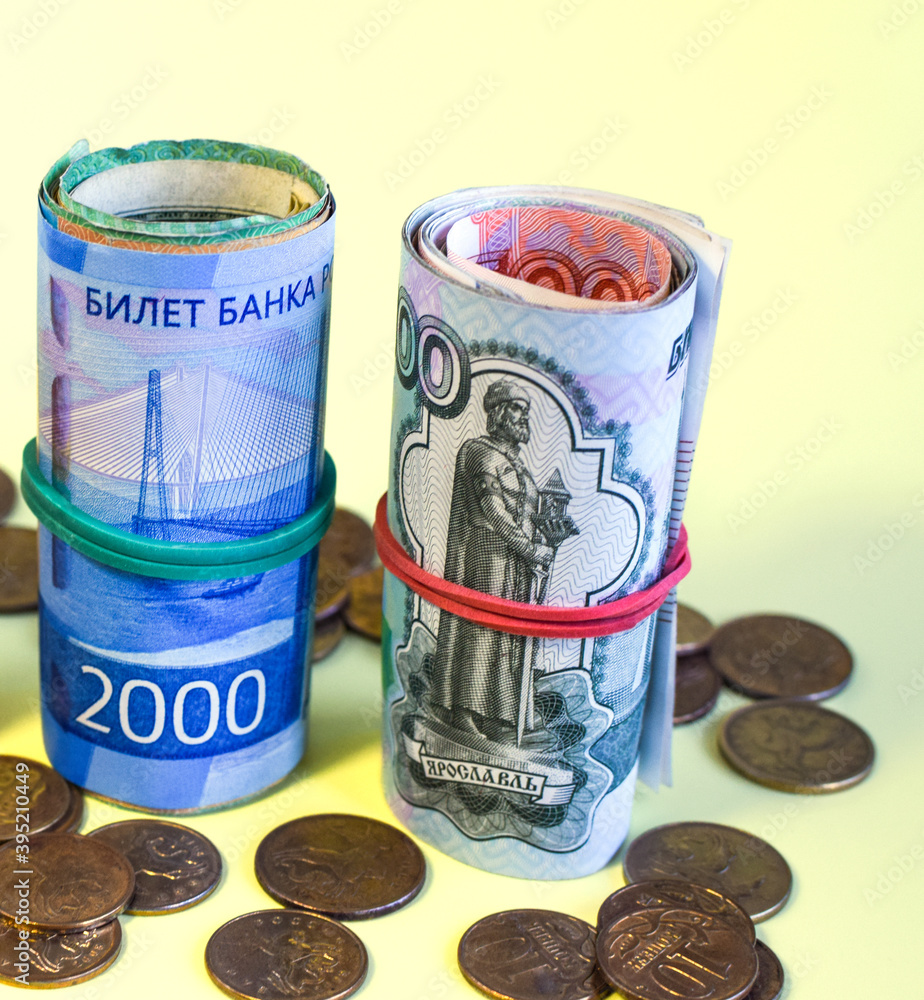 Russian rubles rolled into a tube and metal coins on a light background ...
