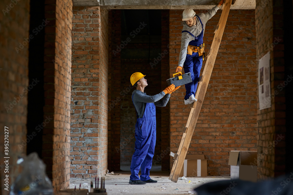 Assistance. Full length shot of young workman in blue overalls and hard ...