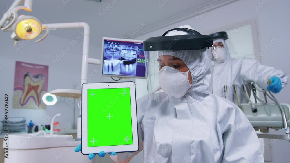 Doctor in ppe suit showing tablet with green screen, explaining dental ...