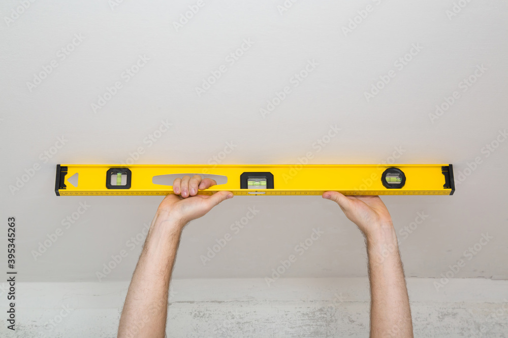 Worker hands measuring white ceiling surface with yellow spirit level ...