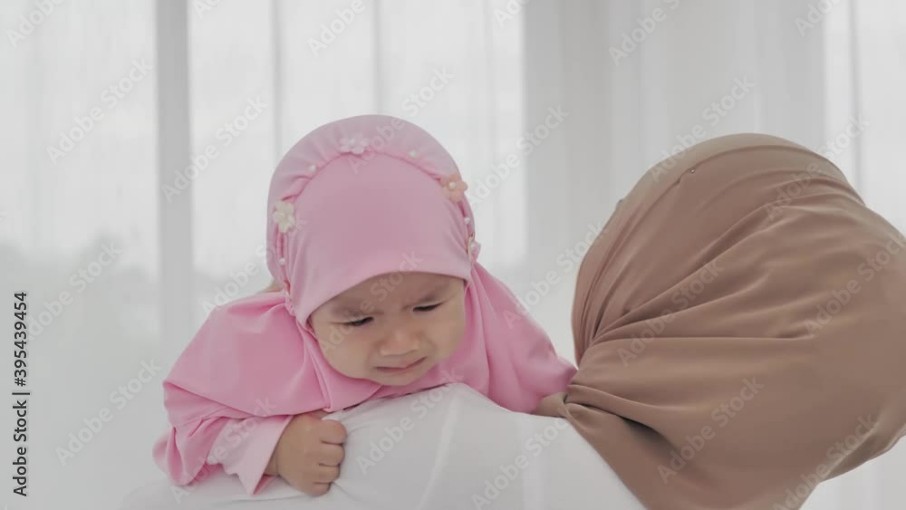 A young Muslim mother is holding a crying infant daughter on her ...