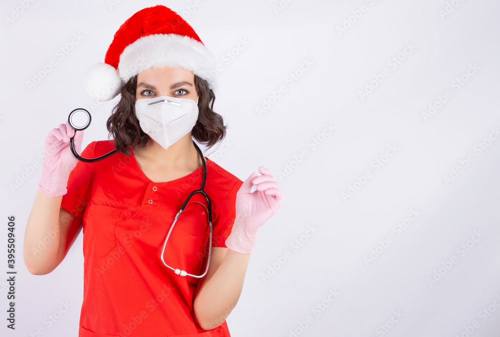 A young female doctor in a uniform, medical mask and Santa hat with a ...