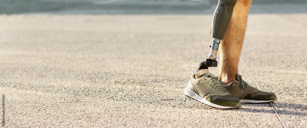 Low angle view at disabled young man with prosthetic leg walking along ...