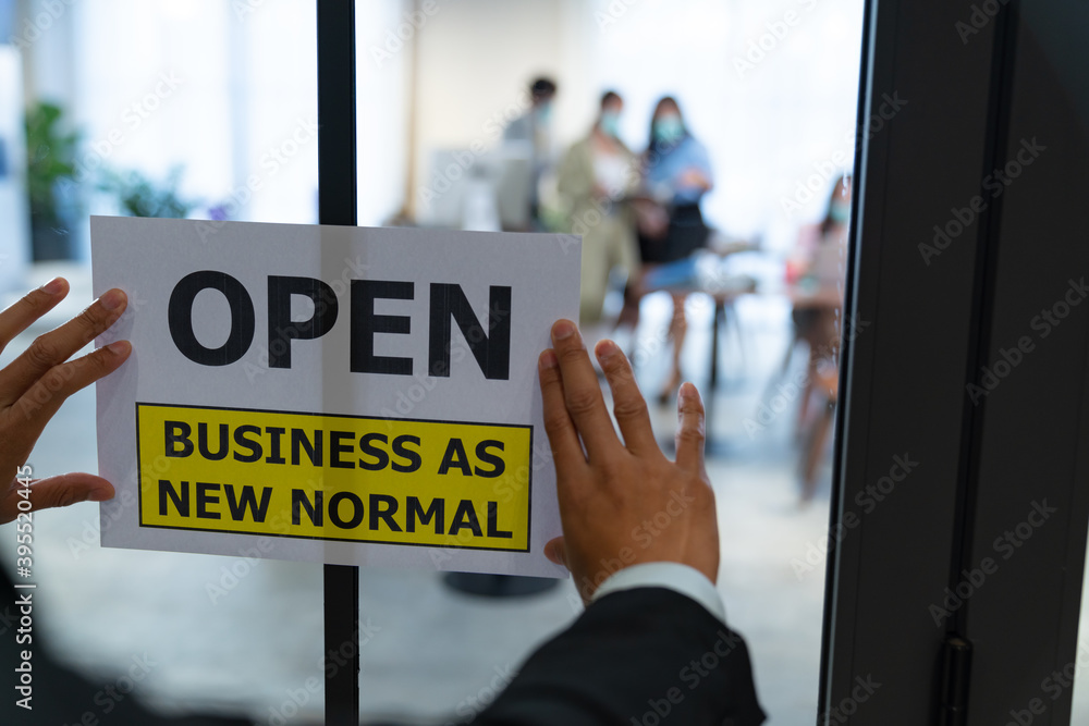 A businessman wearing a surgical mask puts an open sign "Open" at the ...