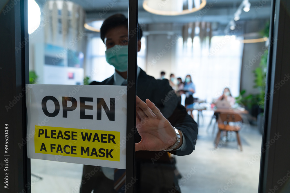 A businessman wearing a surgical mask puts an open sign "Open" at the ...