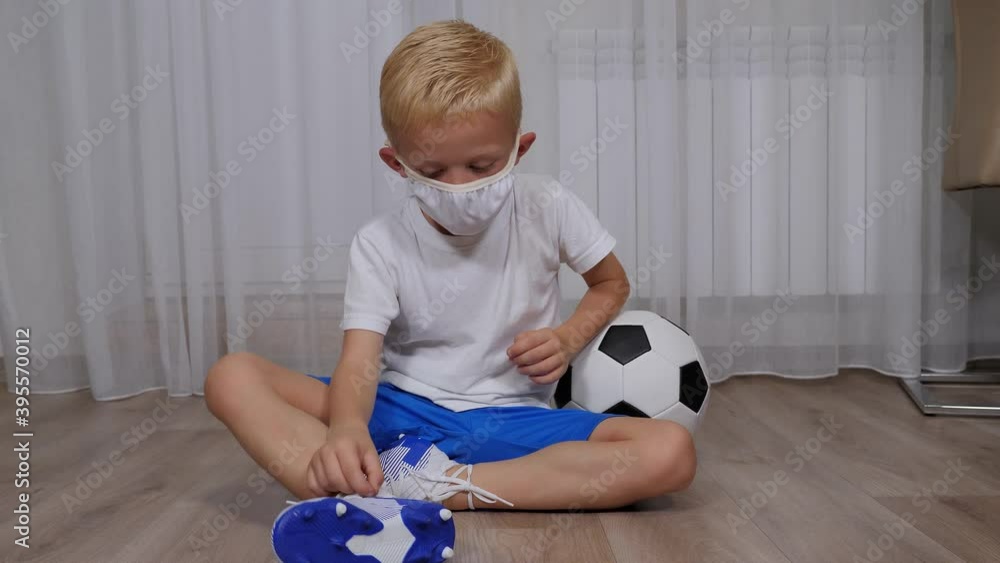Sad boy in soccer uniform is bored at home sitting on the floor with a ...