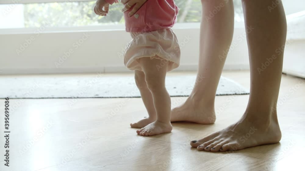 Cute barefoot baby learning walking with help of mother on floor. Side ...