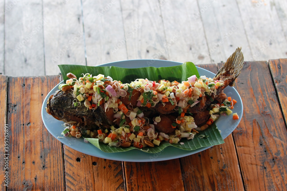 Above view of a whole fried fish served on banana leaf and covered in a ...