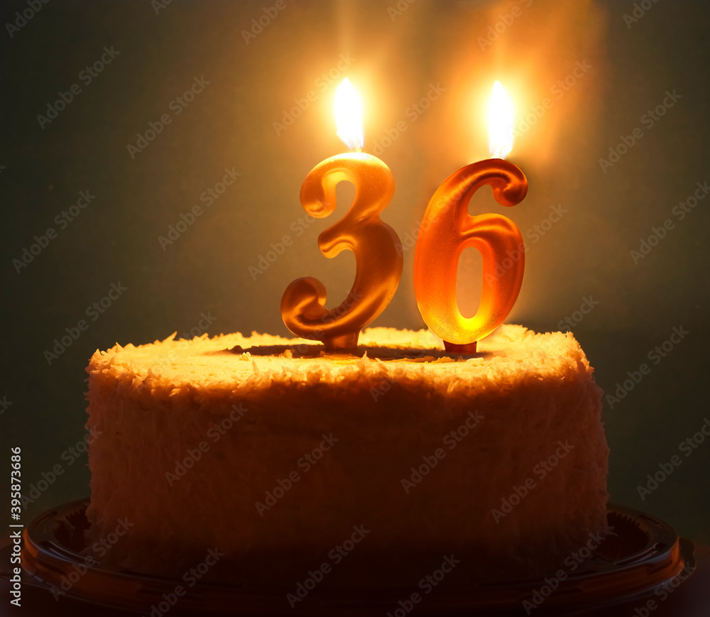 A birthday cake with lit candles and the number 36 on it.night scene ...