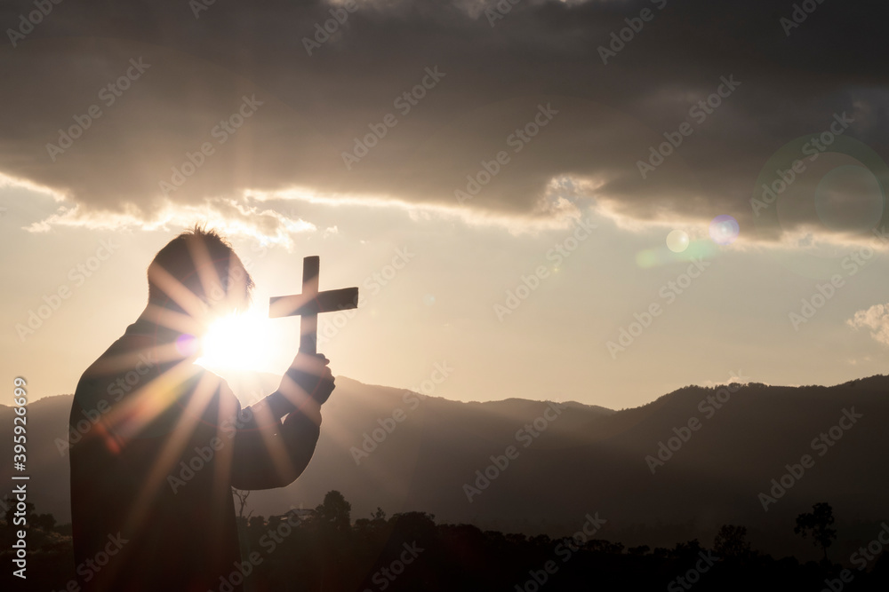 Silhouette of human kneeling down praying and holding christian cross ...